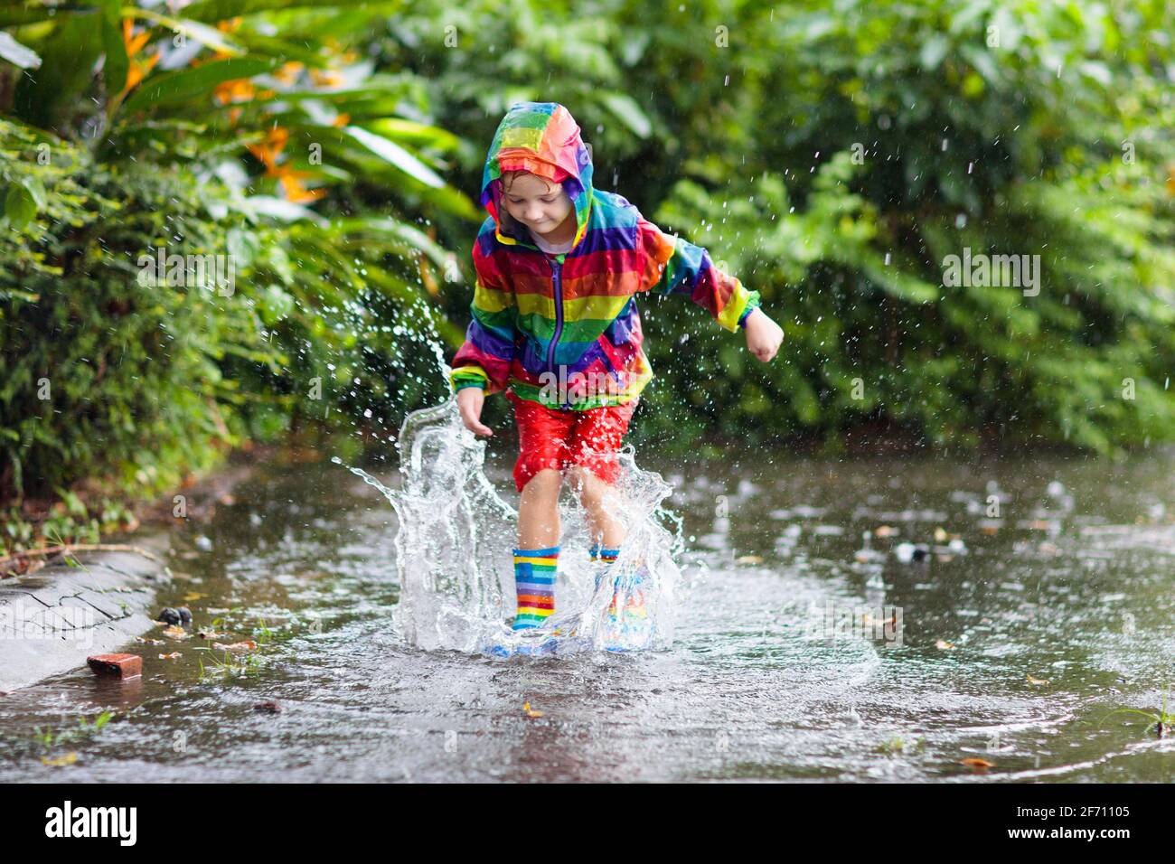 Kid playing in the rain in autumn park. Child jumping in muddy puddle ...