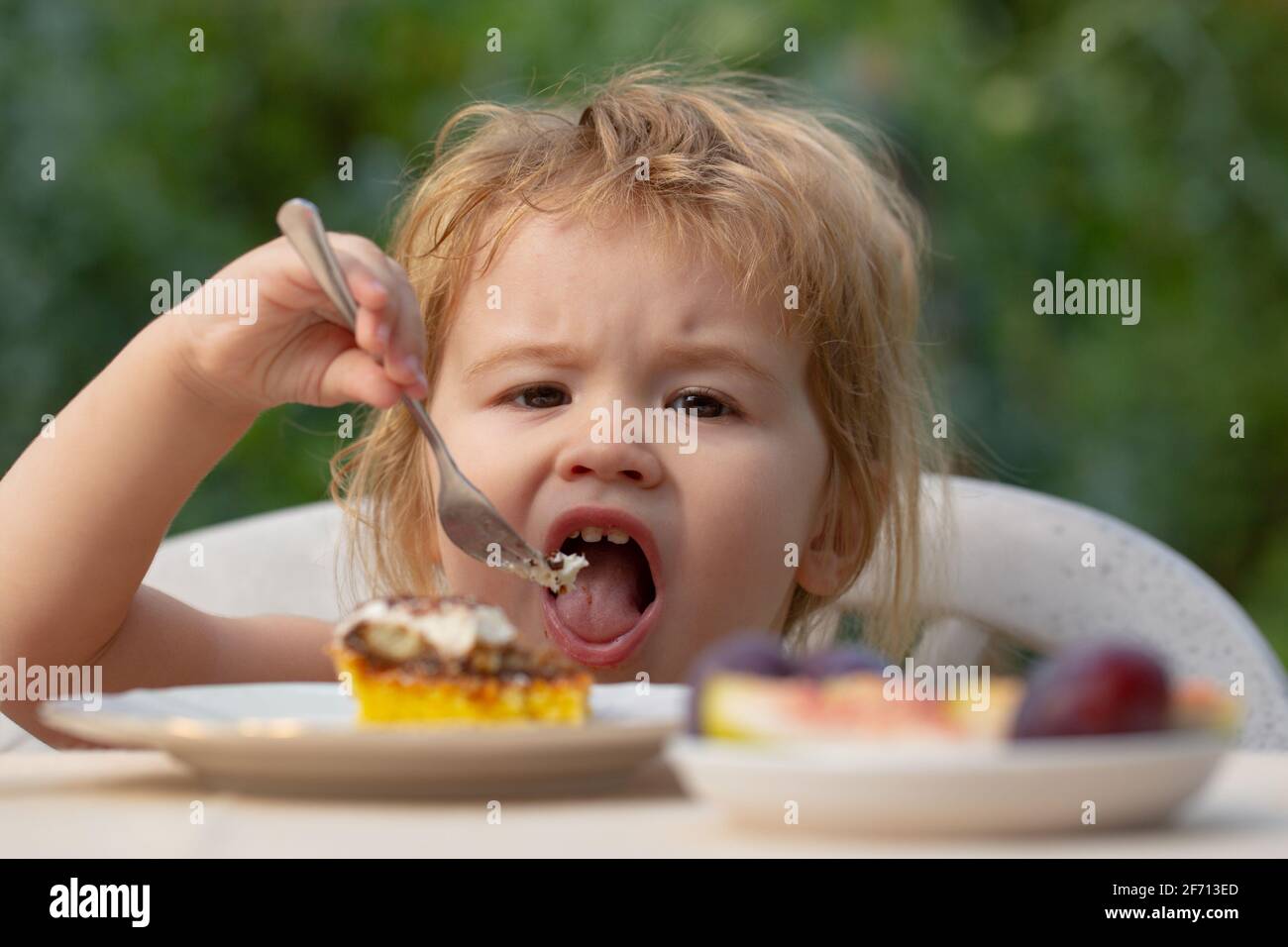Feeding kids. Child eating cake in the garden outside in summer. Baby ...