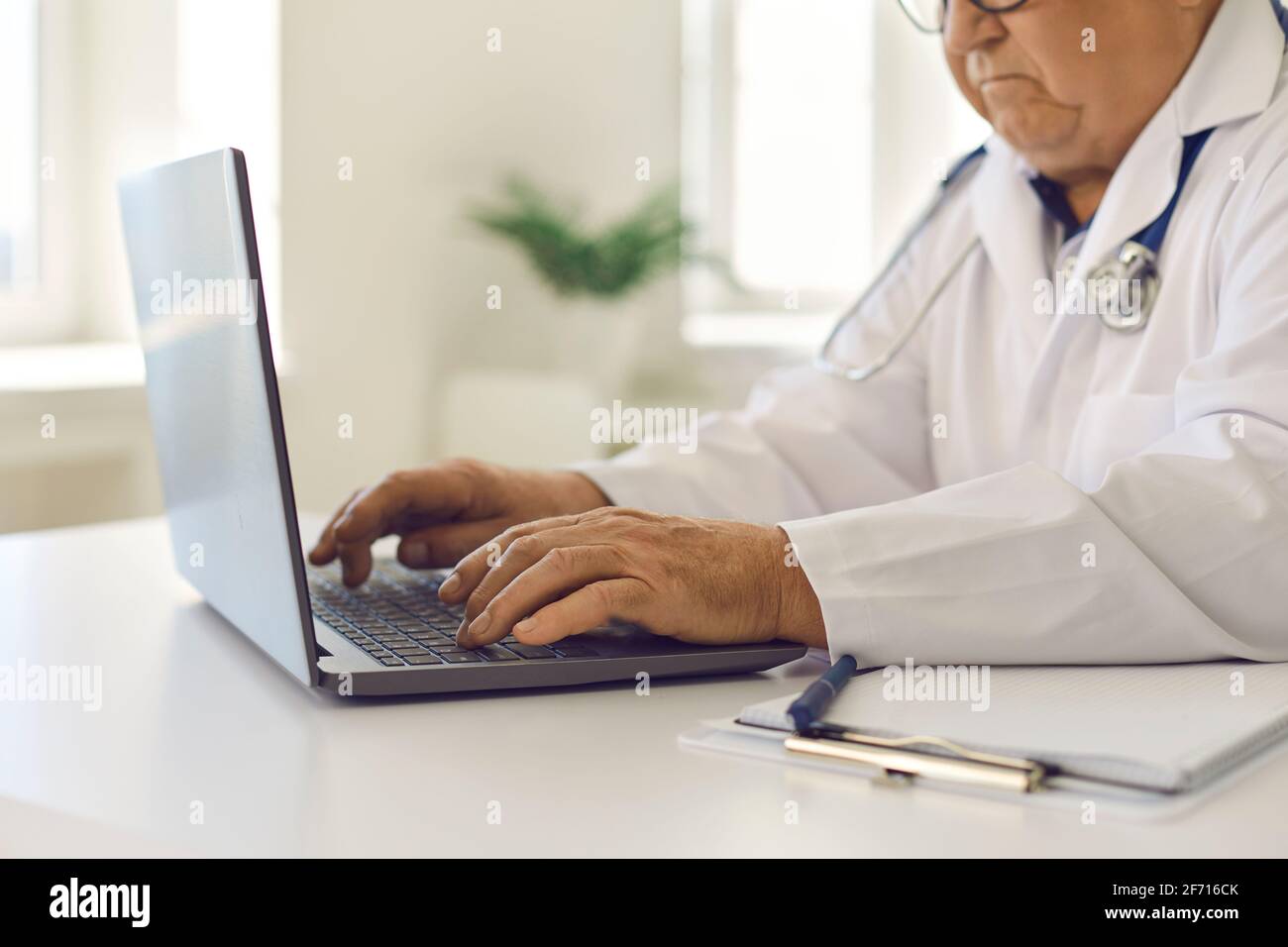 Senior doctor using laptop, giving online consultations to patients or ...