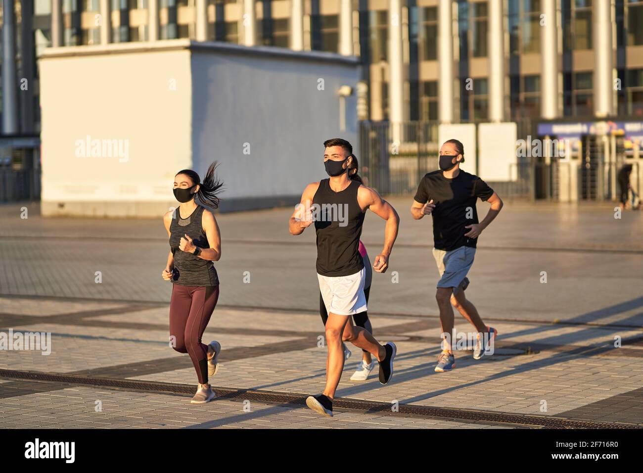 Four athletes in black protective masks on their faces while jogging ...