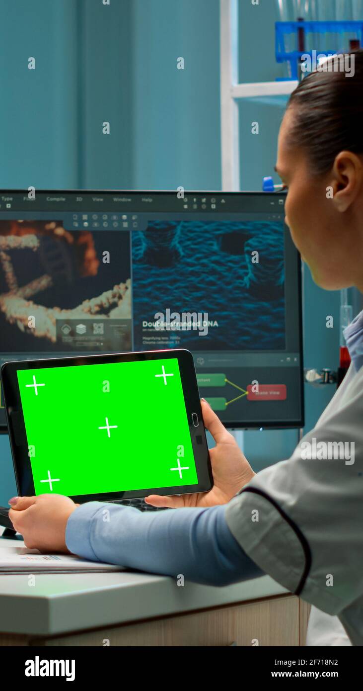 Biochemist sitting at workplace in laboratory using green mock-up screen tablet with chroma key ...