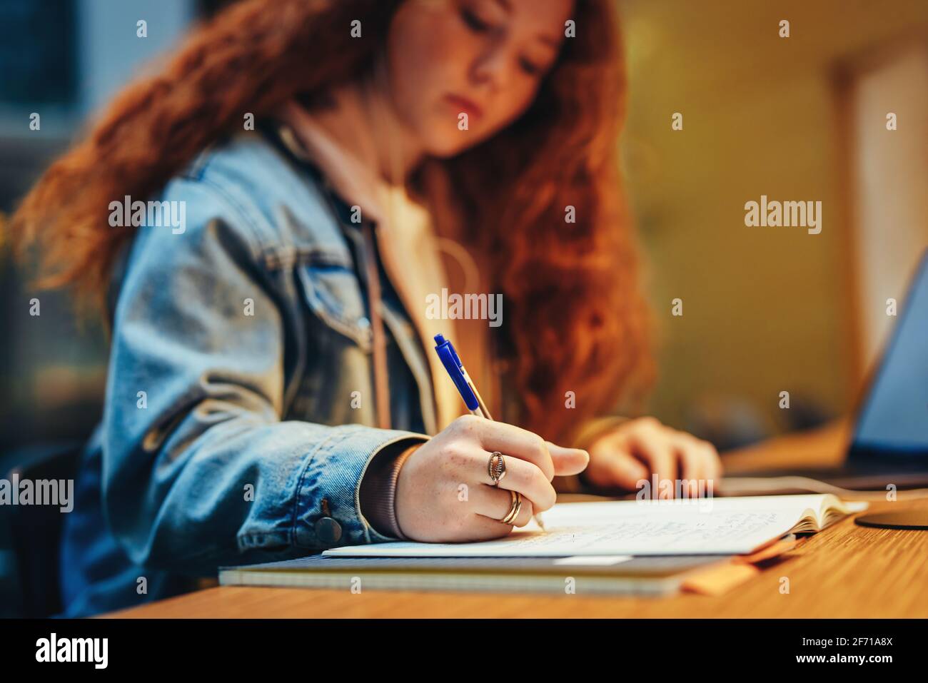 Close-up of a teenage girl making notes in library. Female student ...