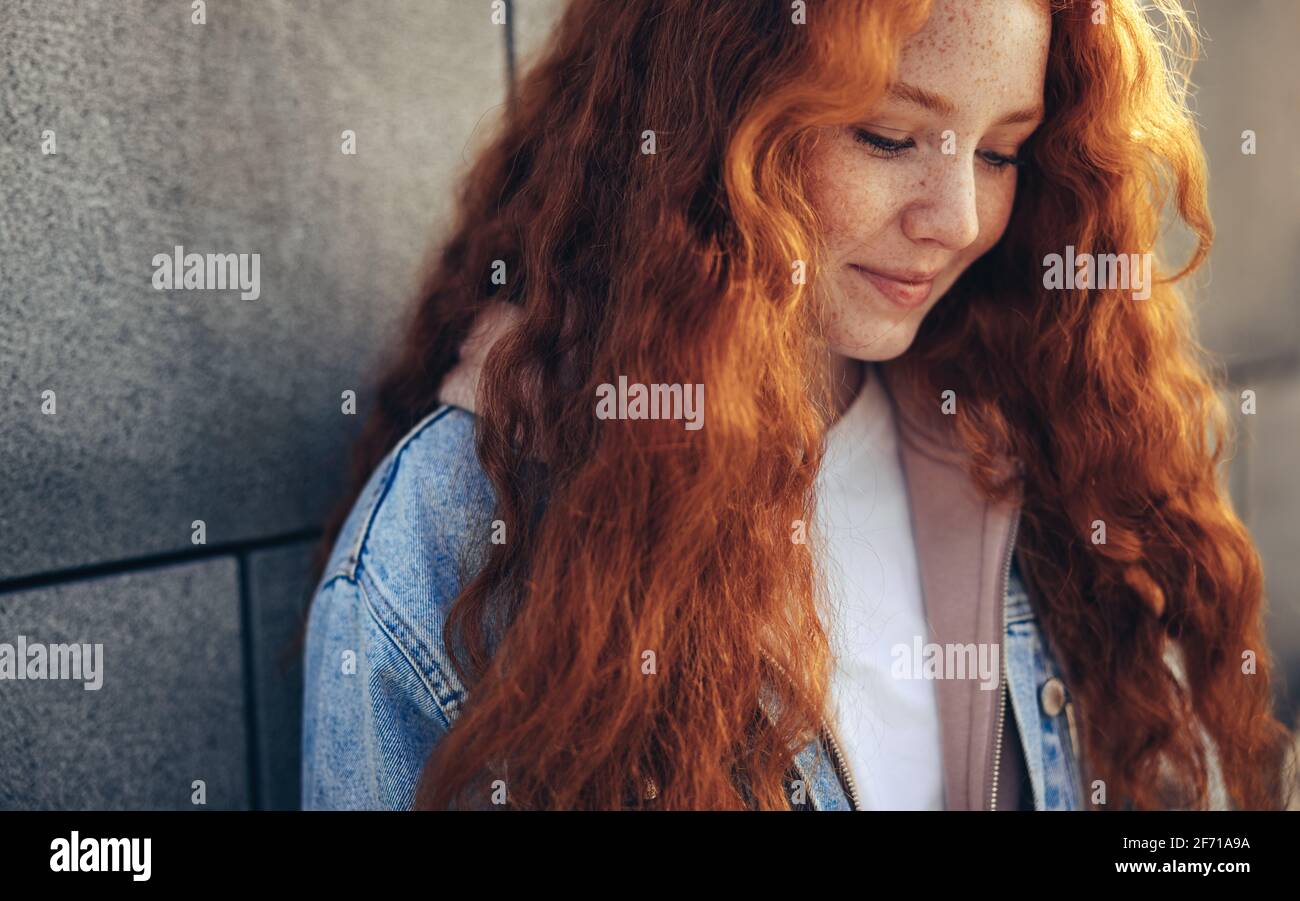 High school student standing against wall and looking down. Young woman ...