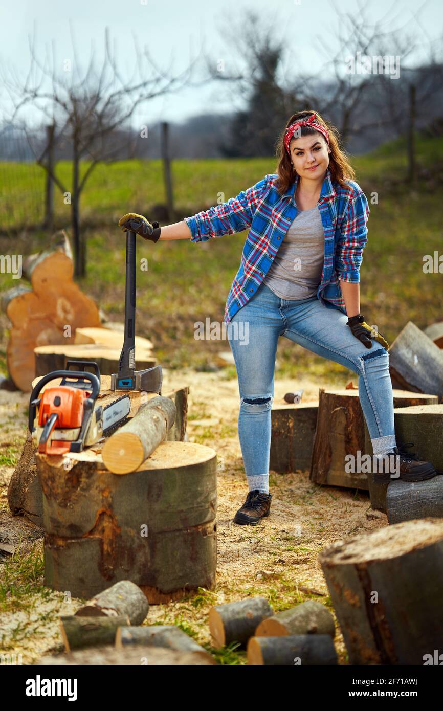 Strong woman woodcutter with her ax and her chainsaw amongst huge sawn ...