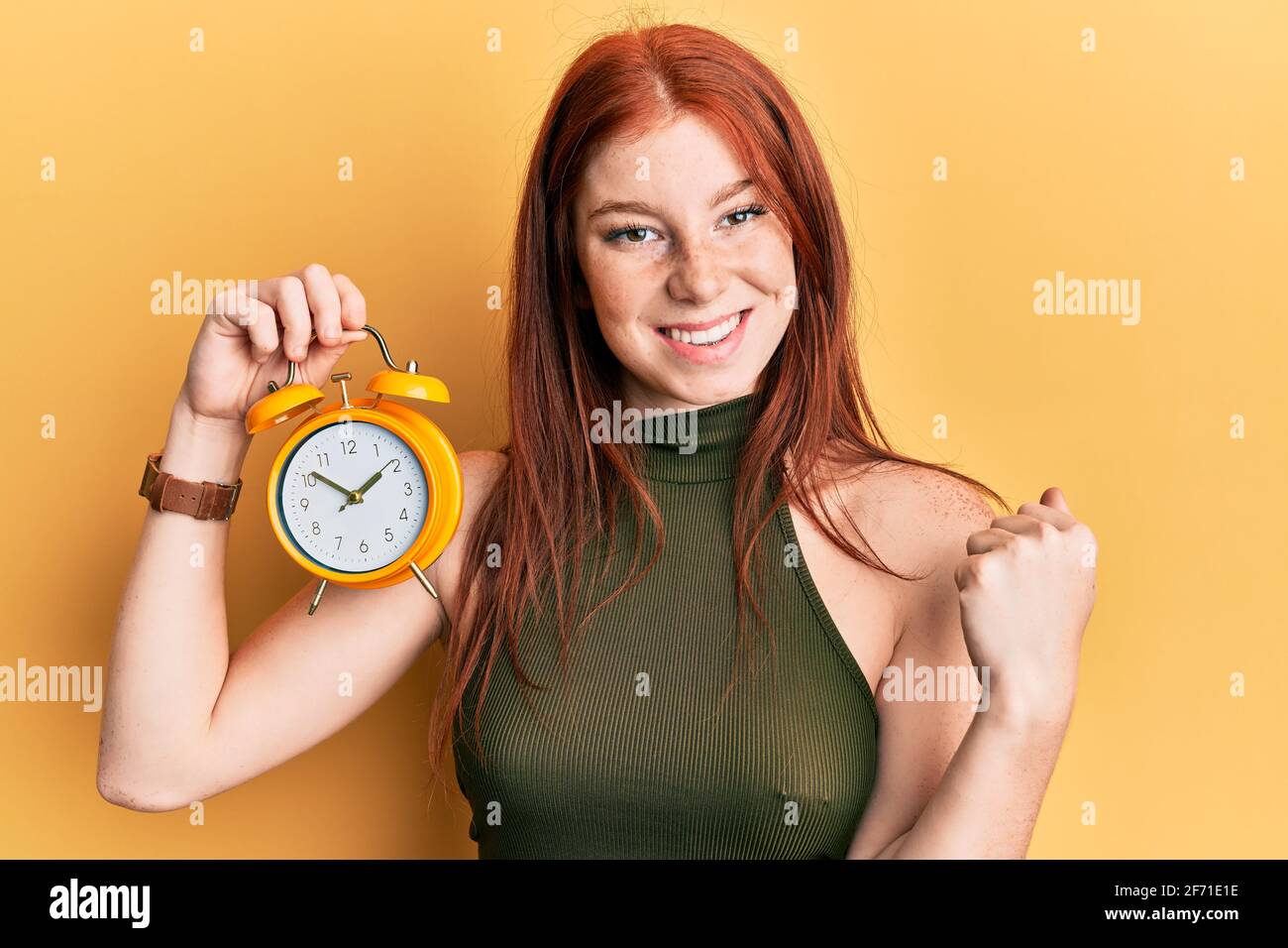 Young red head girl holding alarm clock screaming proud, celebrating ...