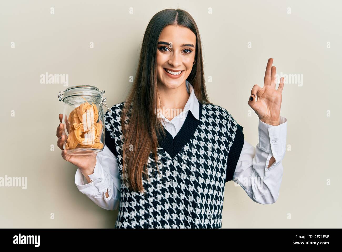 Beautiful brunette young woman holding jar with spaghetti pasta doing ...