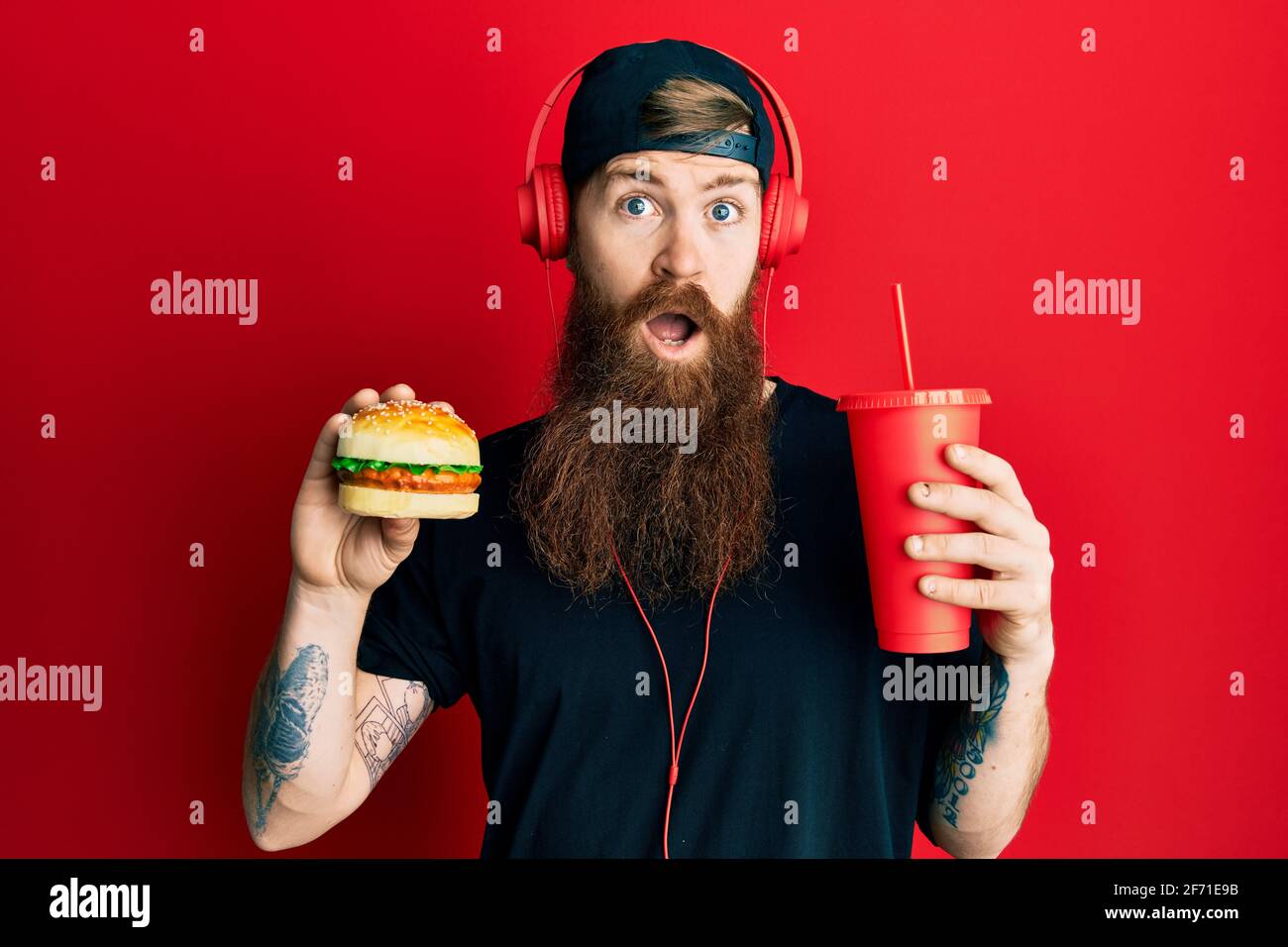 Redhead man with long beard eating a tasty classic burger and drinking ...
