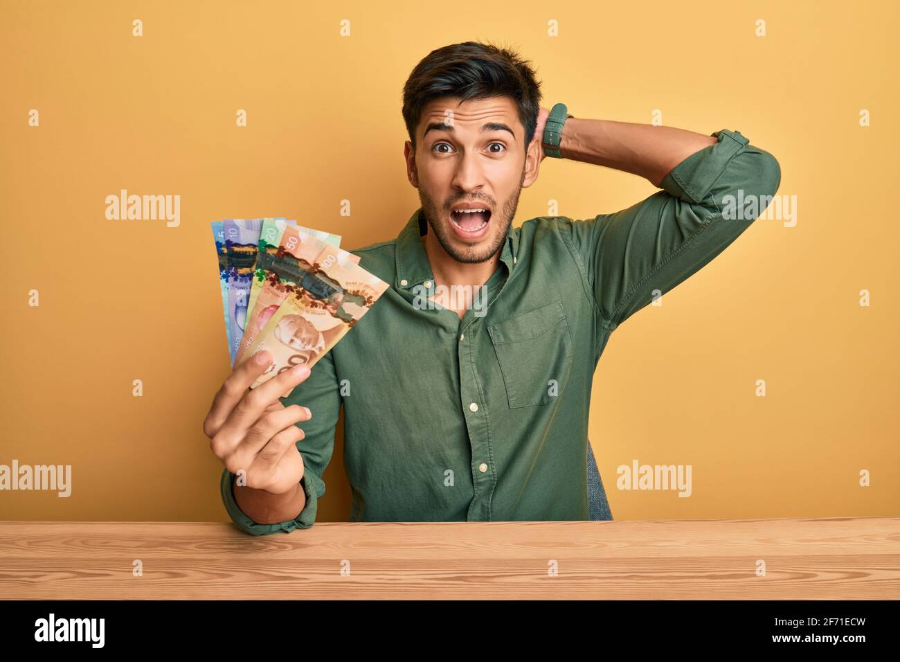 Young handsome man holding canadian dollars crazy and scared with hands ...