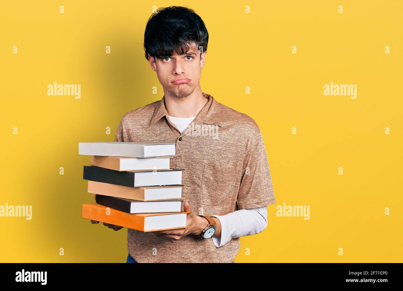 Handsome hipster young man holding a pile of books depressed and worry ...