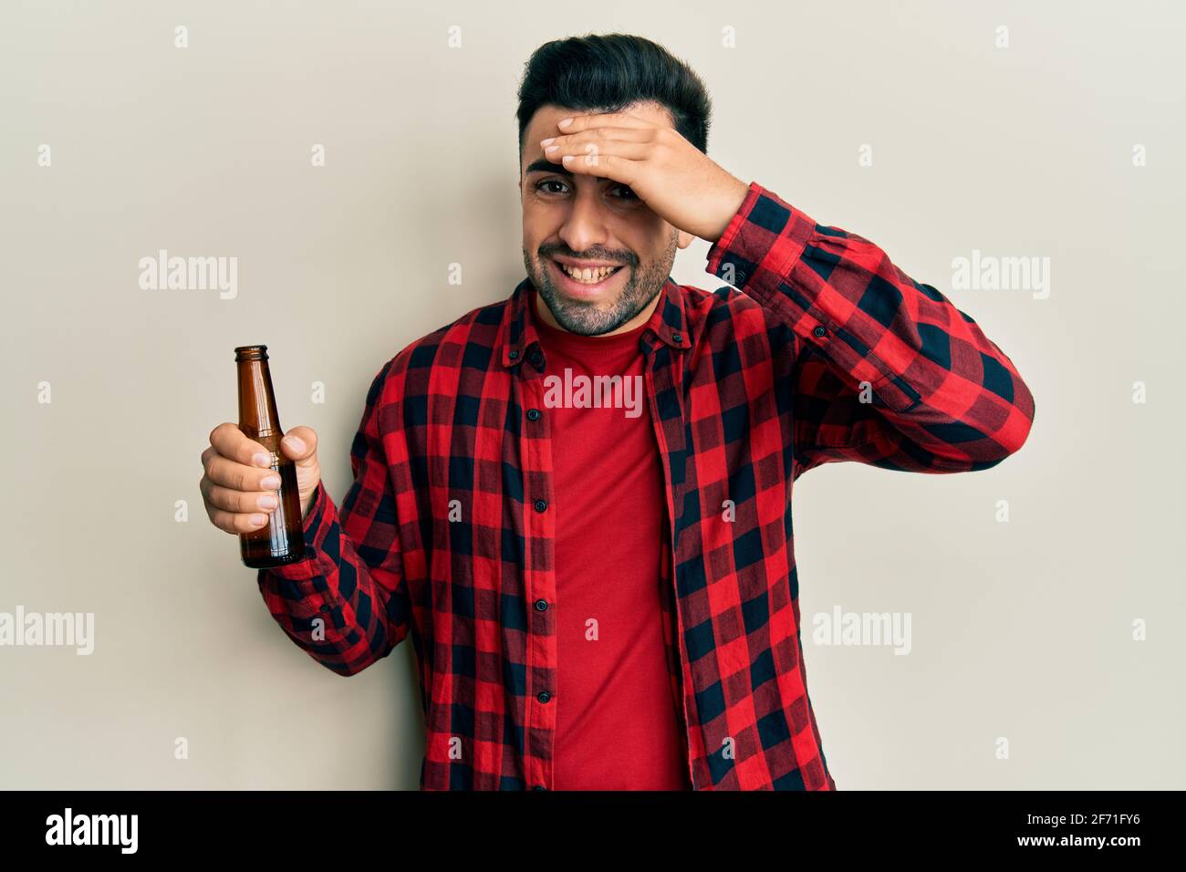 Young hispanic man drinking a bottle of beer stressed and frustrated ...
