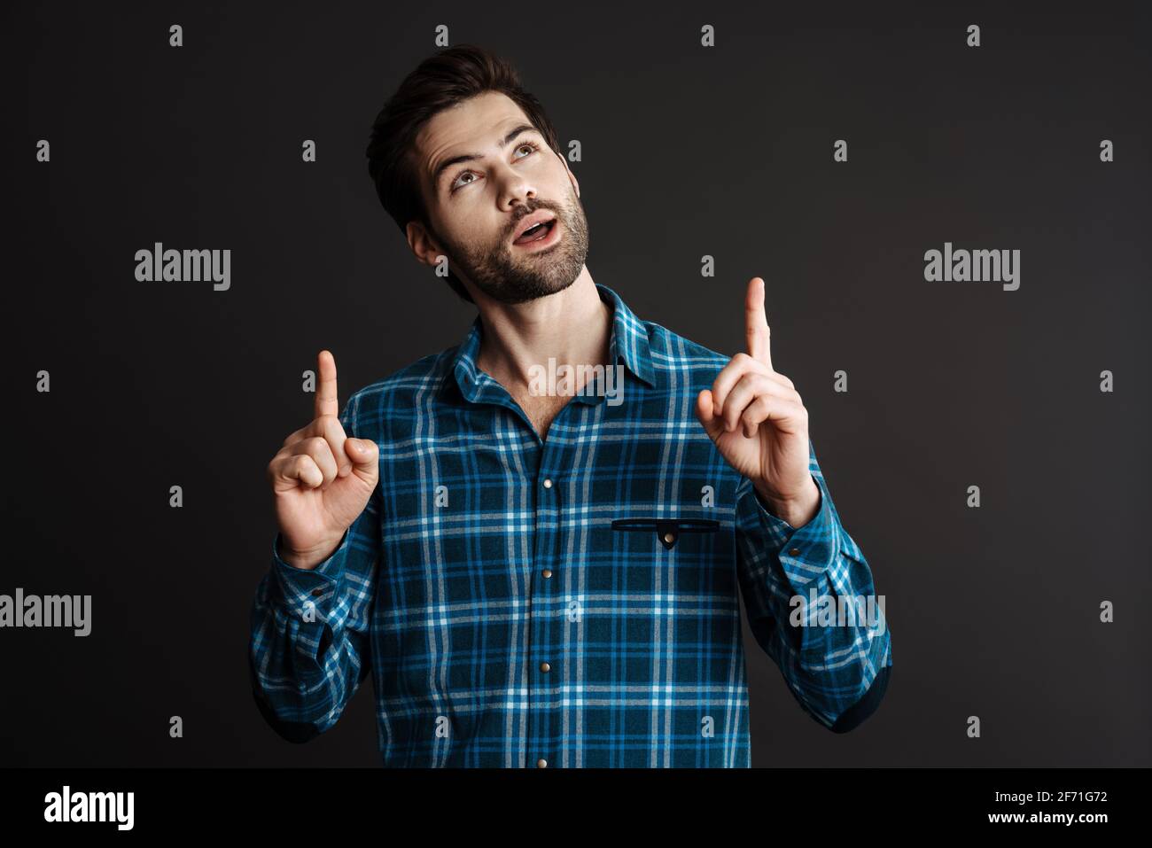 Thinking handsome guy smiling and pointing fingers upward isolated over ...
