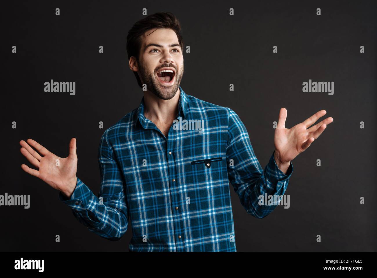 Excited handsome guy posing with throwing up hands isolated over black ...