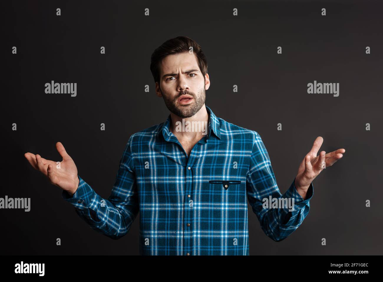 Confused handsome unshaven guy posing with hands up isolated over black ...