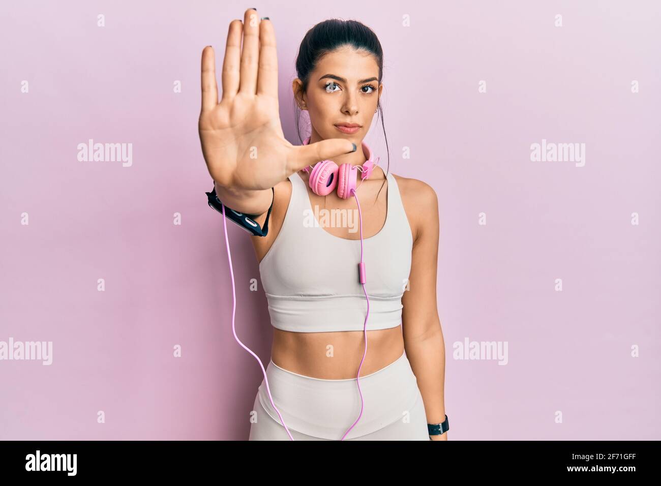 Young hispanic woman wearing gym clothes and using headphones doing ...