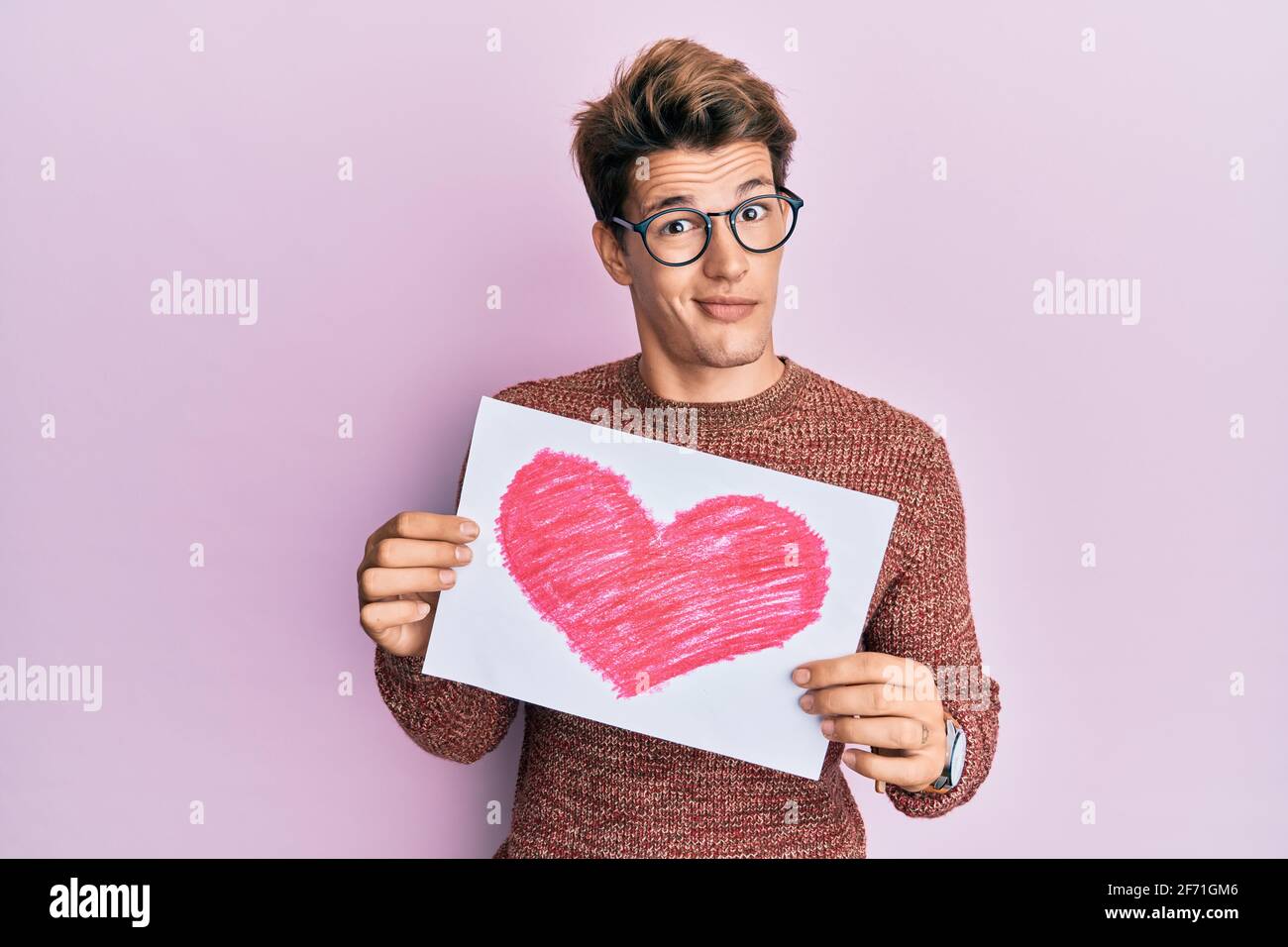 Handsome caucasian man holding heart draw skeptic and nervous, frowning ...