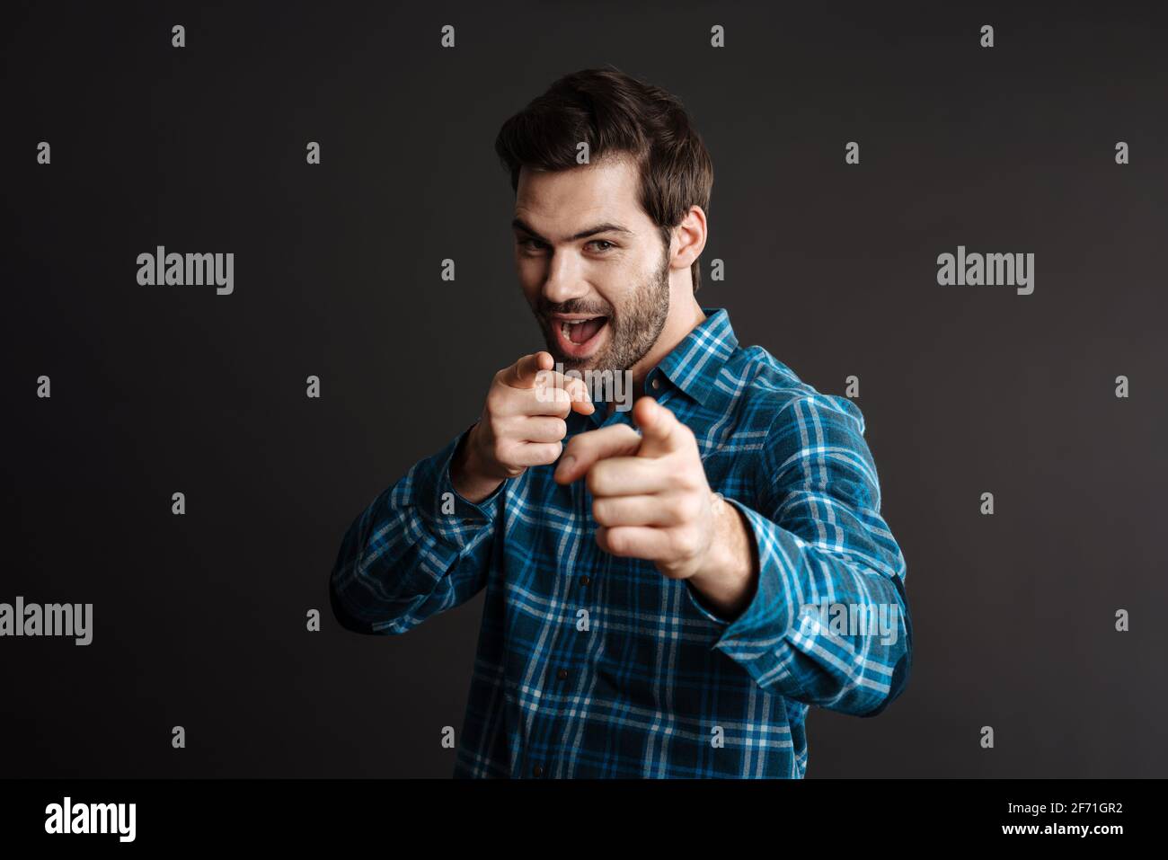 Excited handsome brunette guy pointing fingers at camera isolated over ...