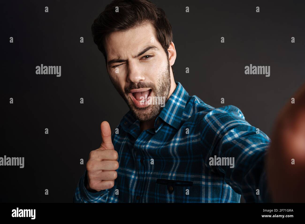 Joyful handsome guy winking and showing thumb up while taking selfie ...