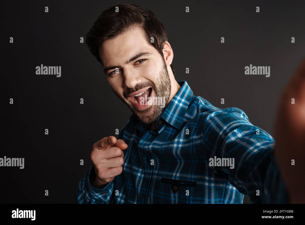 Joyful handsome guy pointing finger at camera while taking selfie ...