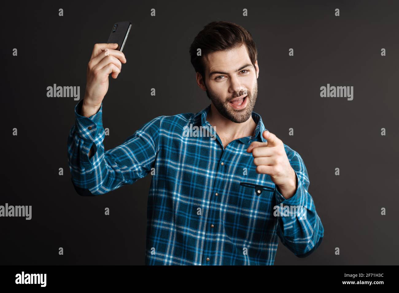 Excited guy pointing finger at camera while taking selfie on cellphone ...