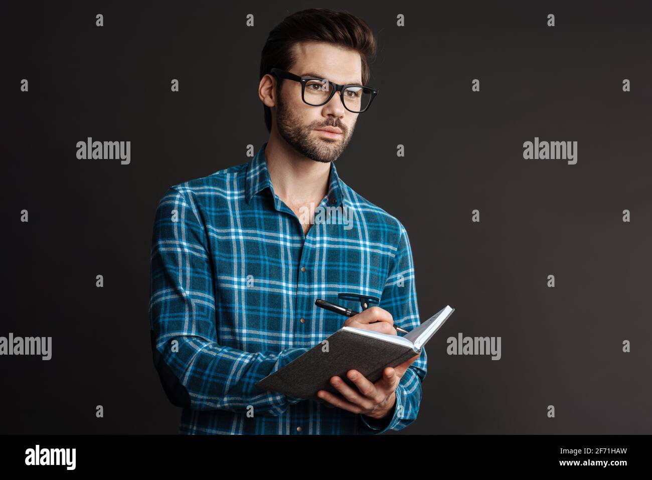 Focused guy in eyeglasses writing down notes in calendar isolated over ...