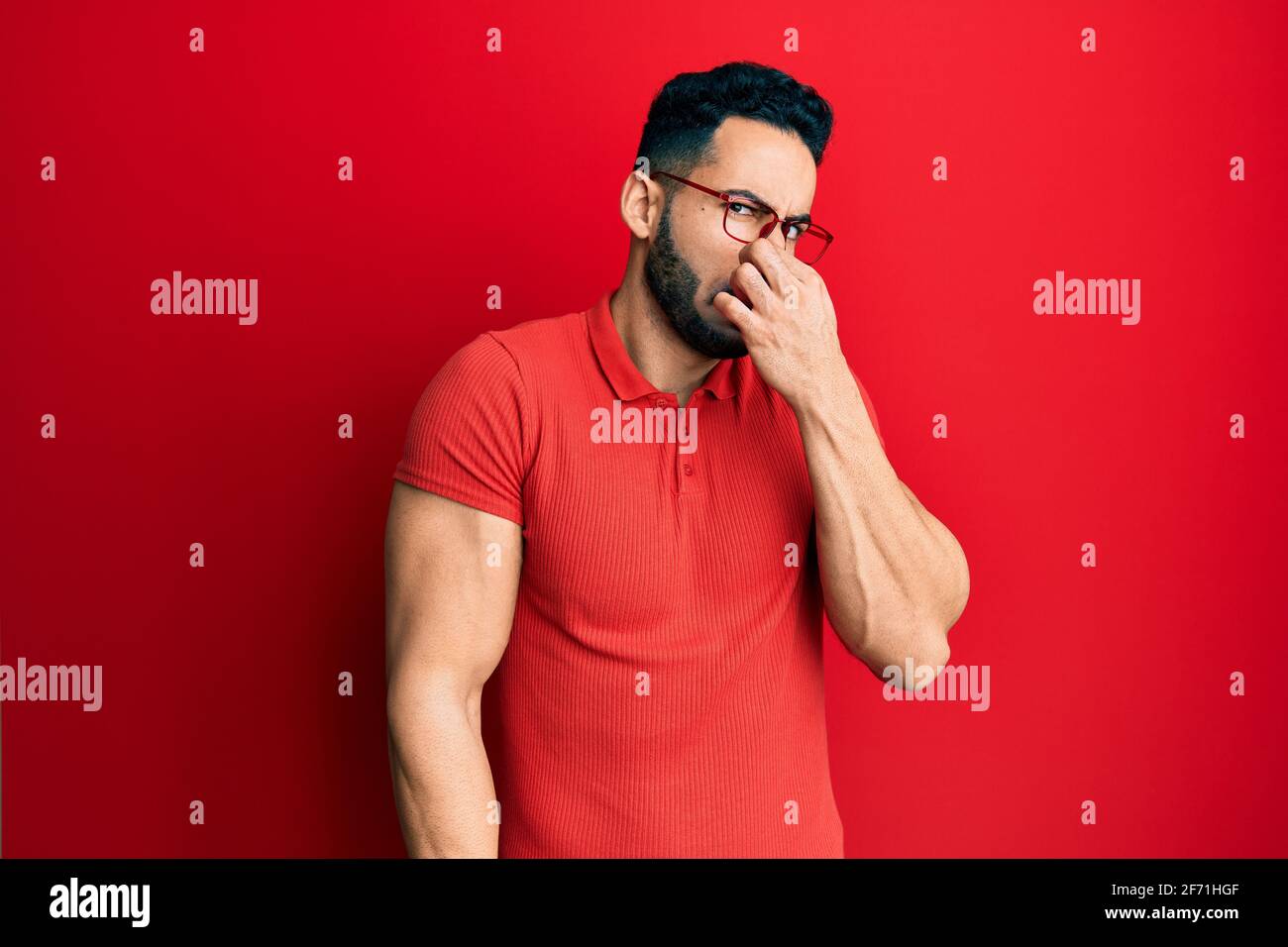 Young hispanic man wearing casual clothes and glasses smelling ...