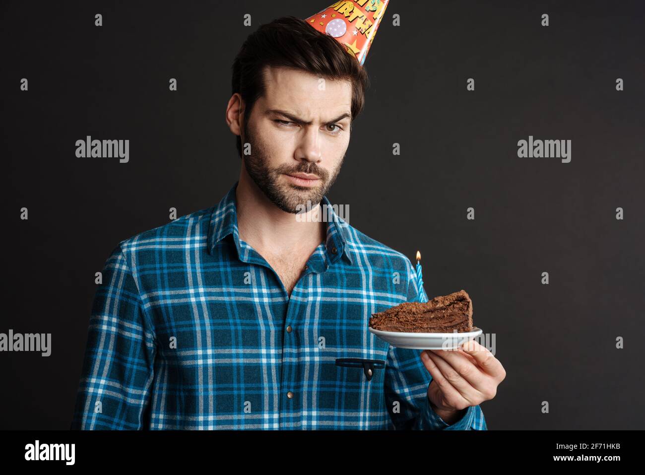 Brooding guy in party cone posing with birthday cake isolated over ...
