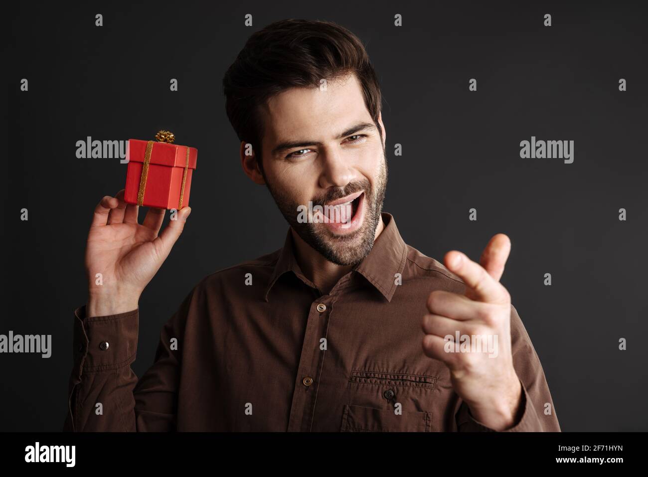 Excited guy holding gift box and pointing finger at camera isolated ...