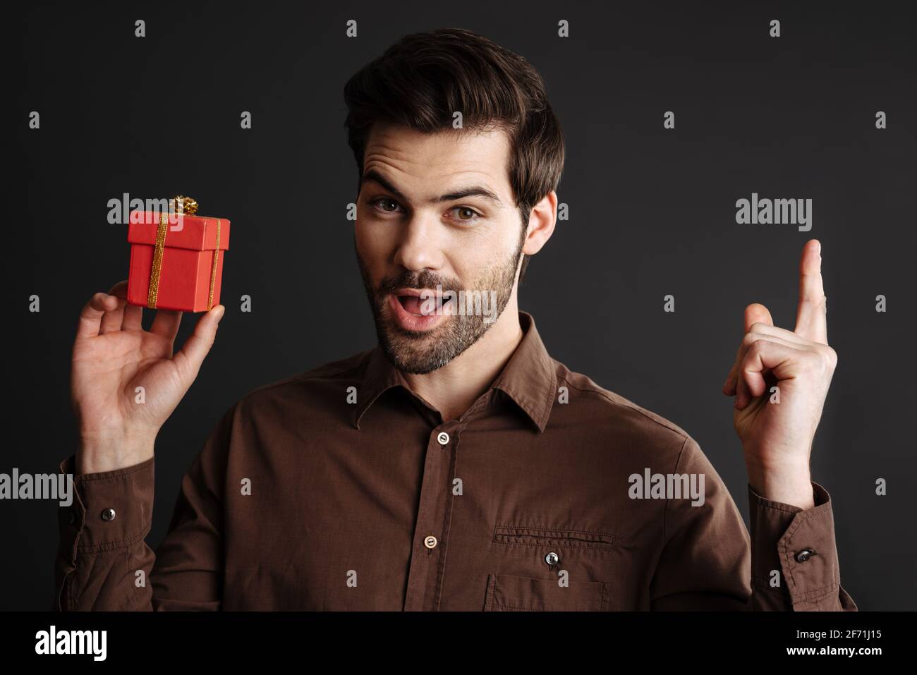 Excited guy holding gift box and pointing finger upward isolated over ...