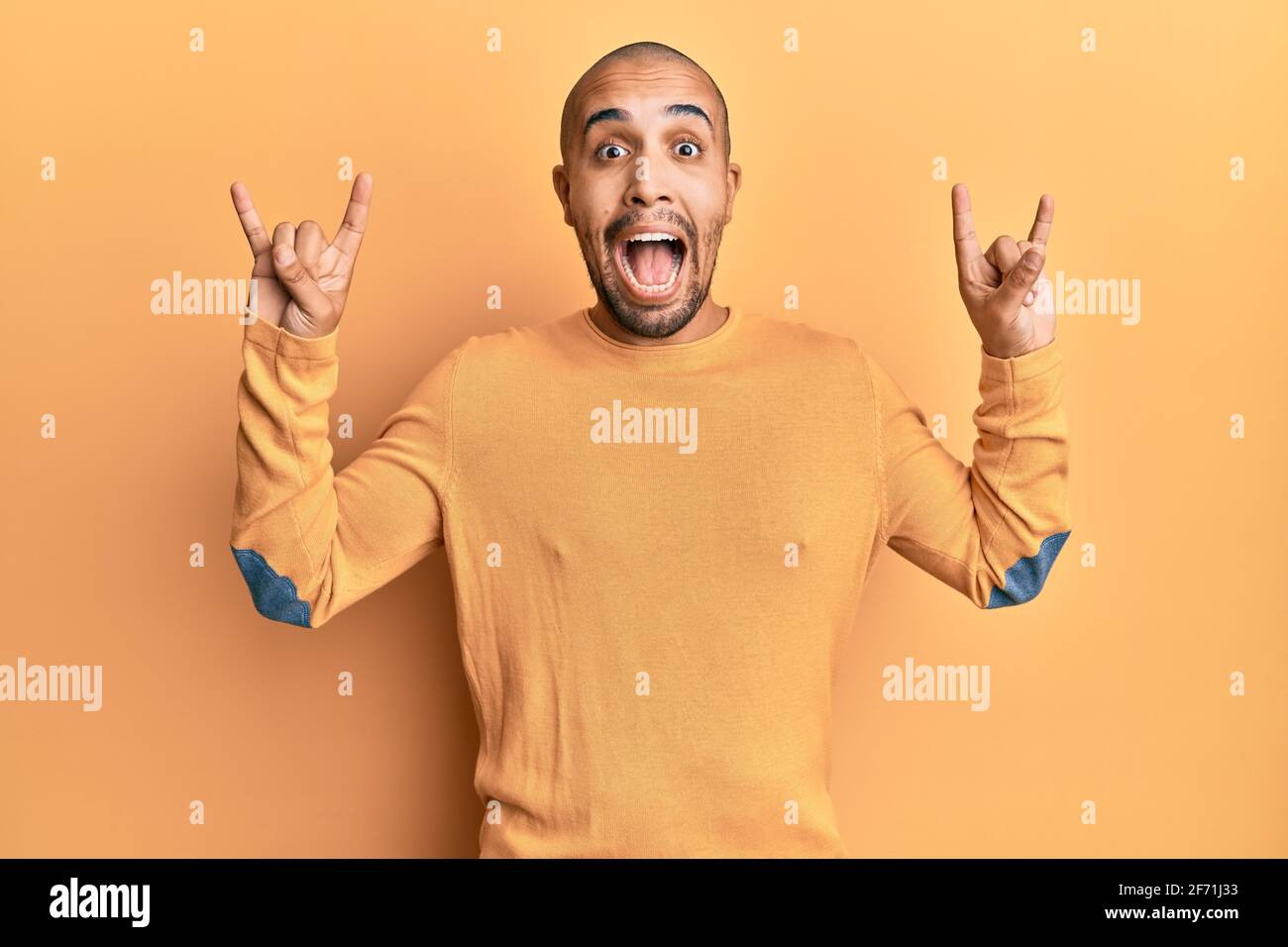 Hispanic adult man doing rock gesture over yellow background ...