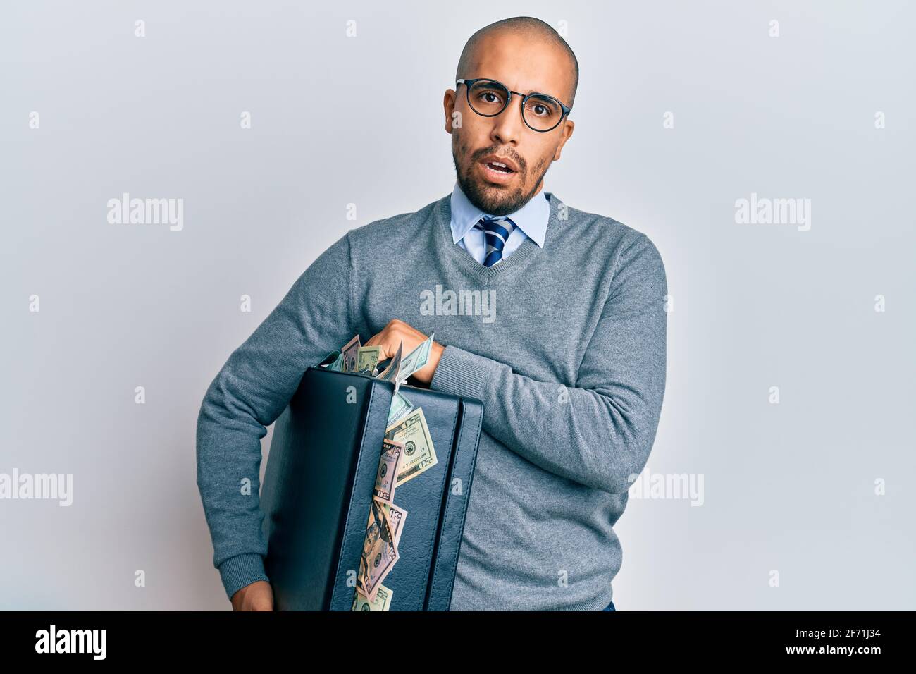 Hispanic adult man holding briefcase full of dollars in shock face ...