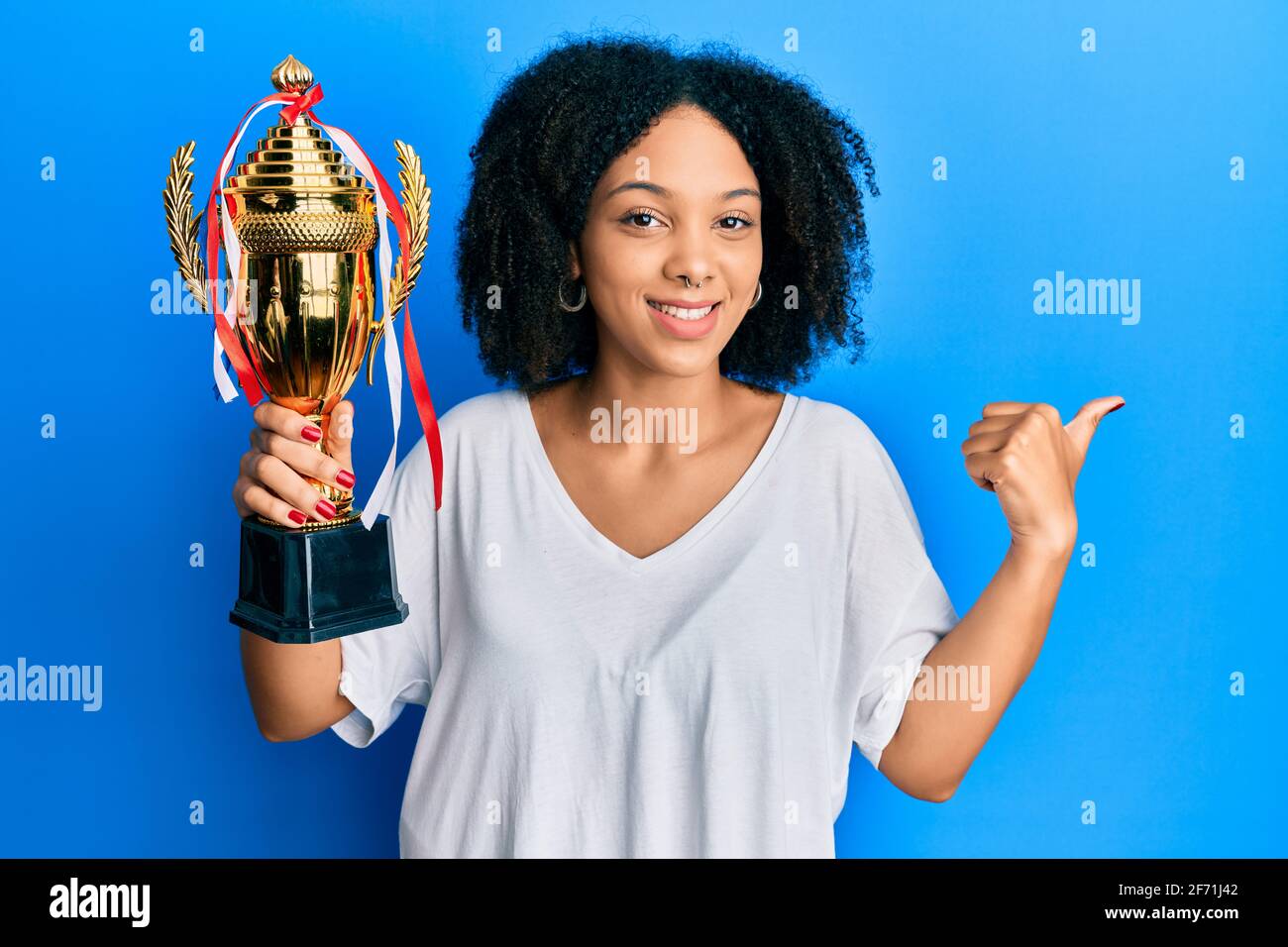 Young african american girl holding winner trophy pointing thumb up to ...