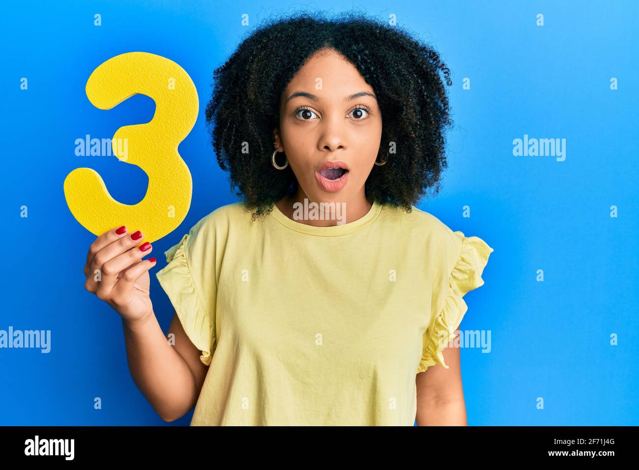 Young african american girl holding number three scared and amazed with ...