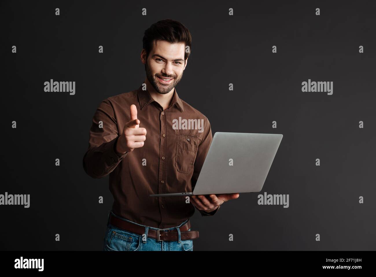Joyful handsome guy using laptop and pointing finger at camera isolated ...