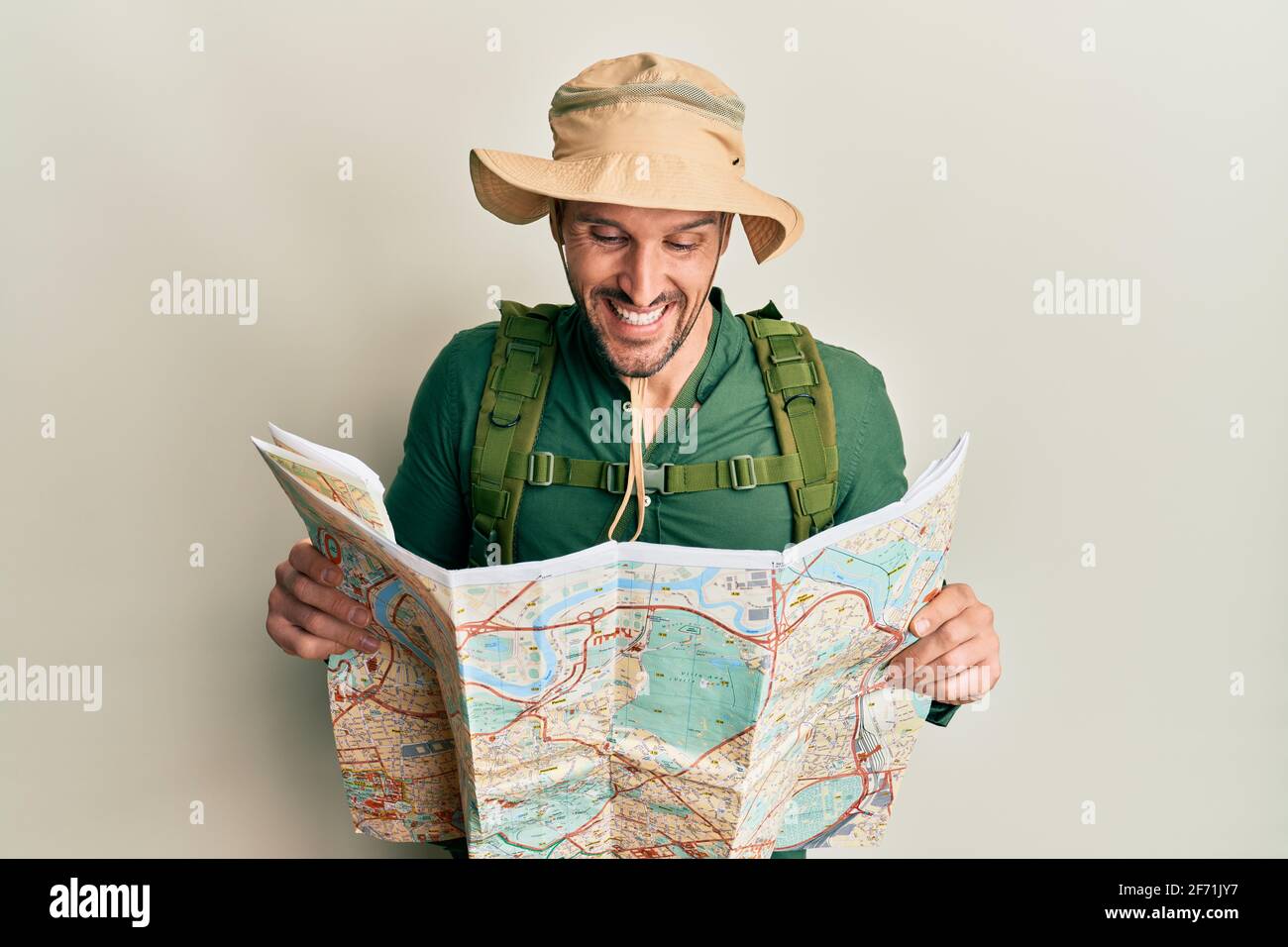 Handsome man with beard wearing explorer hat holding map smiling and ...