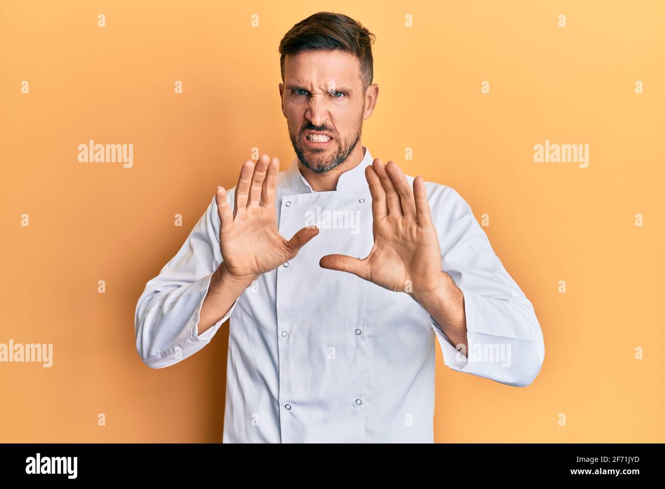 Handsome man with beard wearing professional cook uniform disgusted ...