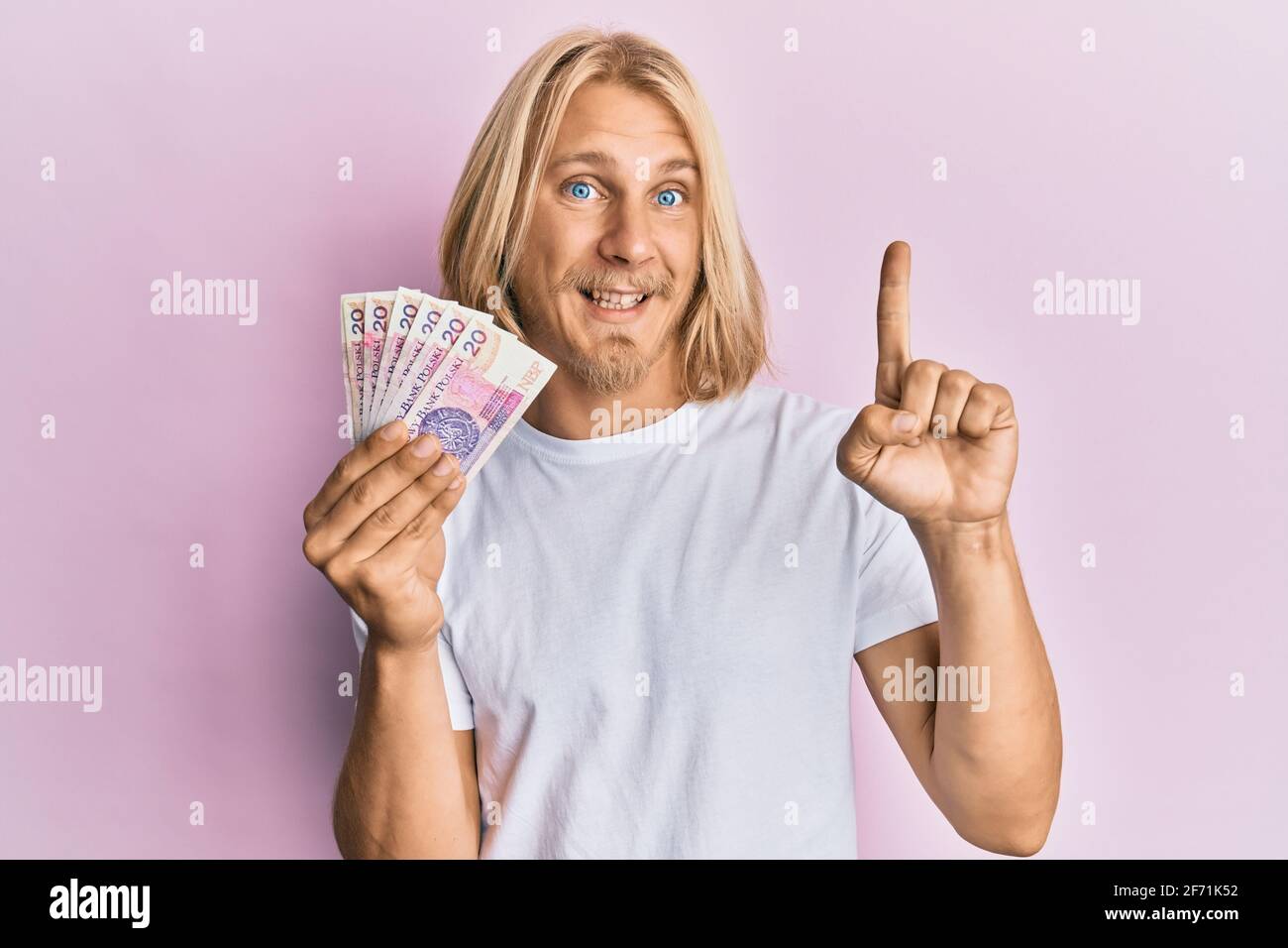 Caucasian young man with long hair holding 20 polish zloty banknotes ...