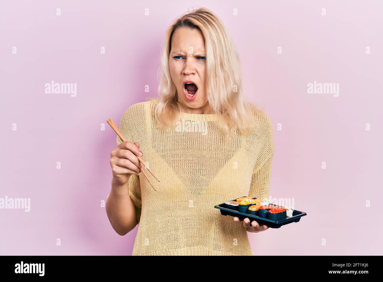 Beautiful caucasian blonde woman eating sushi using chopsticks angry ...