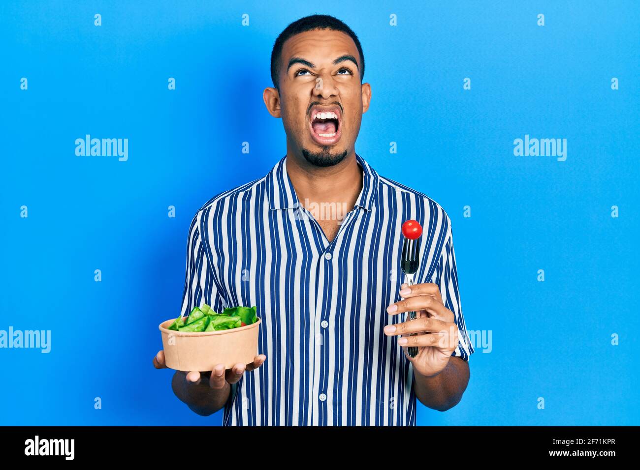 Young african american man eating salad angry and mad screaming ...