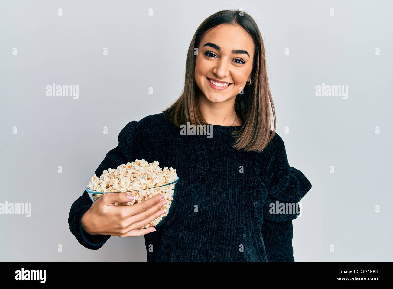 Young brunette girl eating popcorn looking positive and happy standing ...