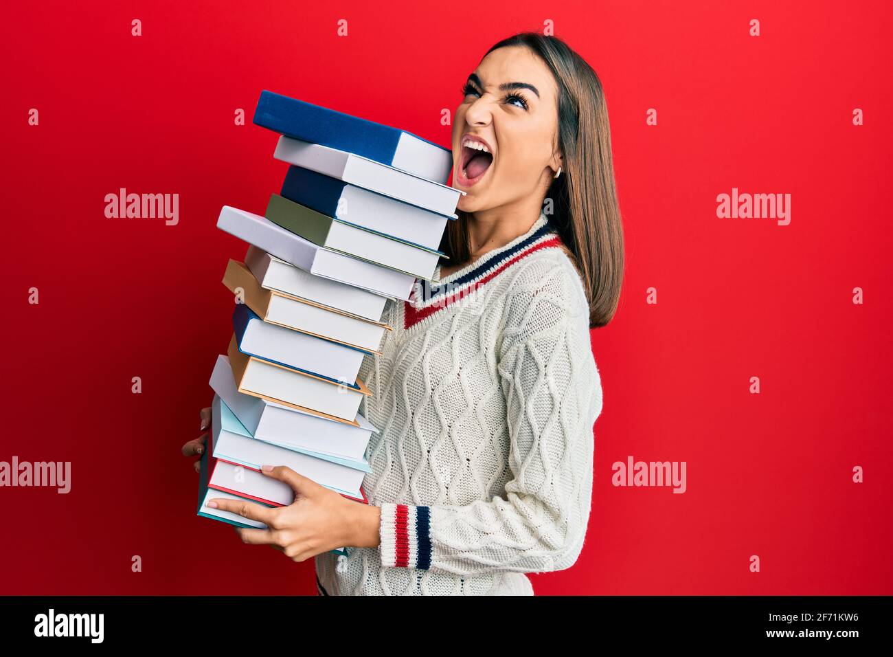 Young brunette student girl holding a pile of books angry and mad ...