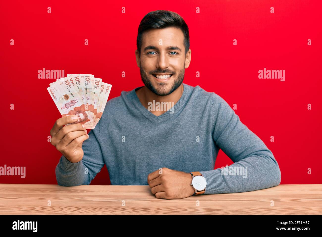 Handsome hispanic man holding colombian pesos looking positive and ...