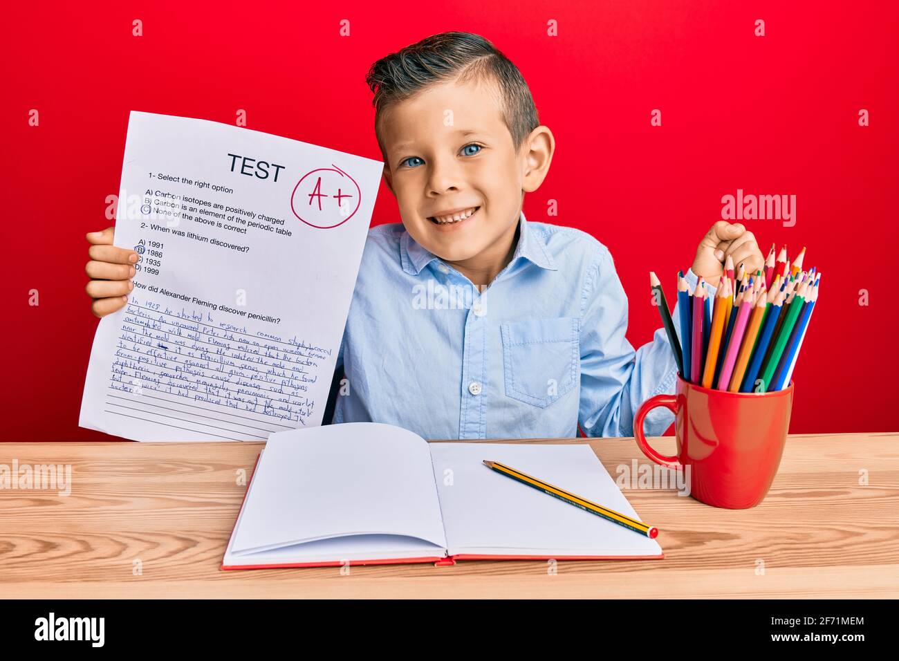 Adorable caucasian kid holding passed test sitting on the table ...