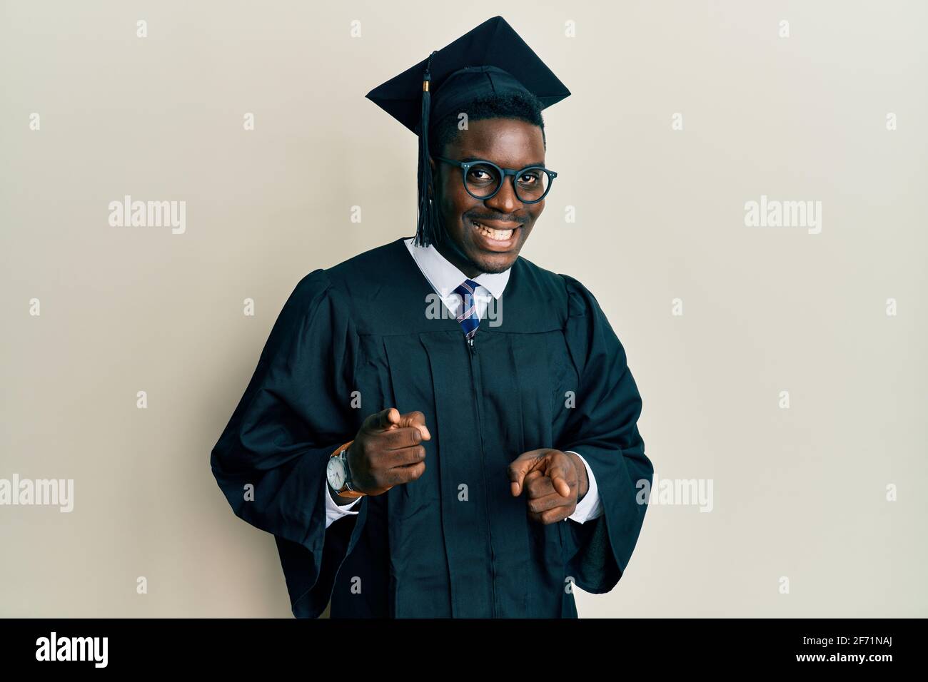 Handsome black man wearing graduation cap and ceremony robe pointing ...