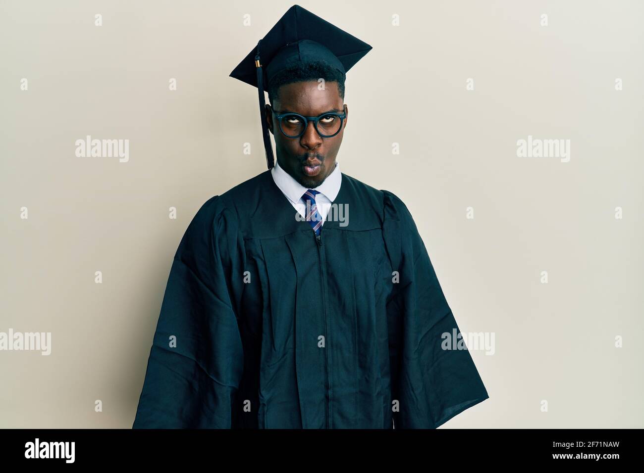Handsome black man wearing graduation cap and ceremony robe making fish ...