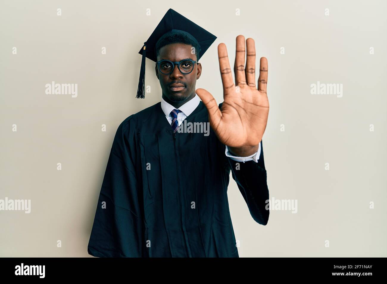 Handsome black man wearing graduation cap and ceremony robe doing stop ...