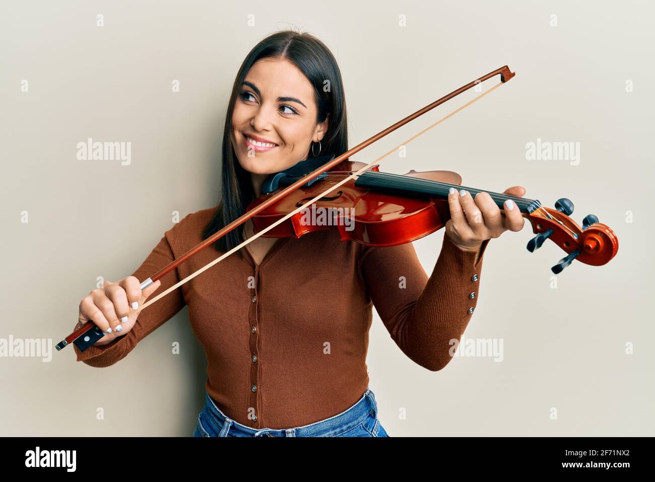 Young brunette woman playing violin smiling looking to the side and ...