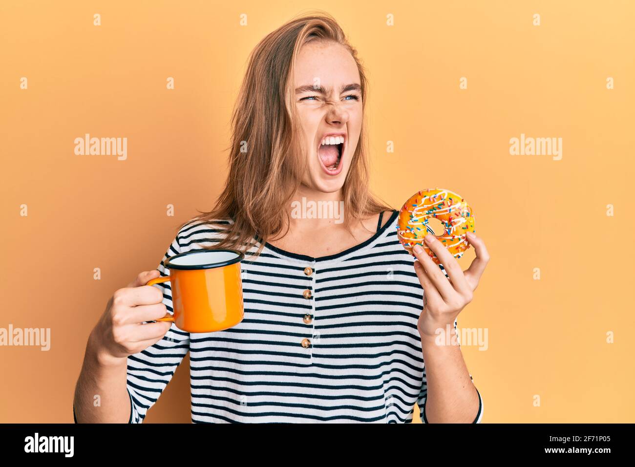 Beautiful blonde woman eating doughnut and drinking coffee angry and ...