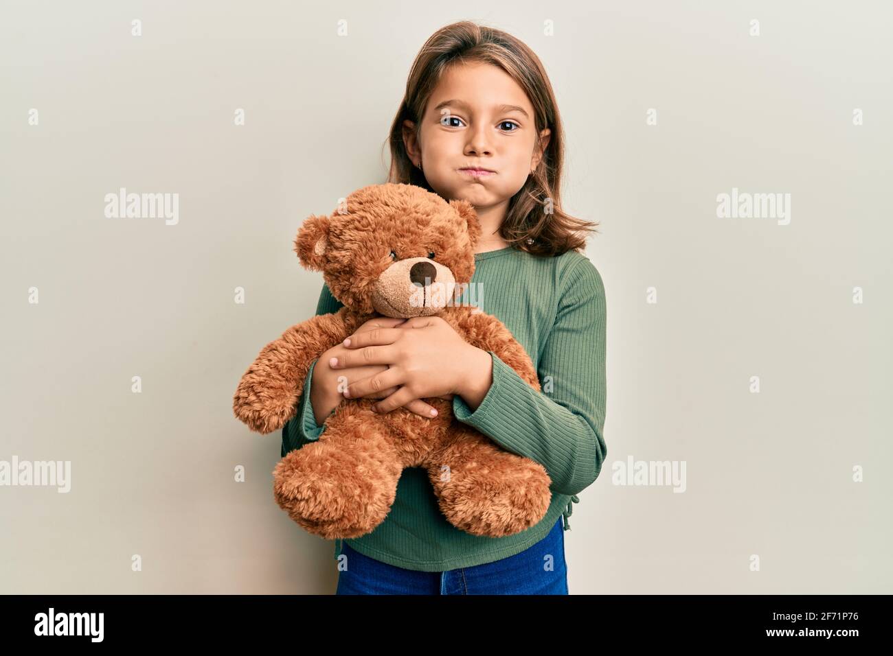 Little beautiful girl hugging teddy bear puffing cheeks with funny face ...