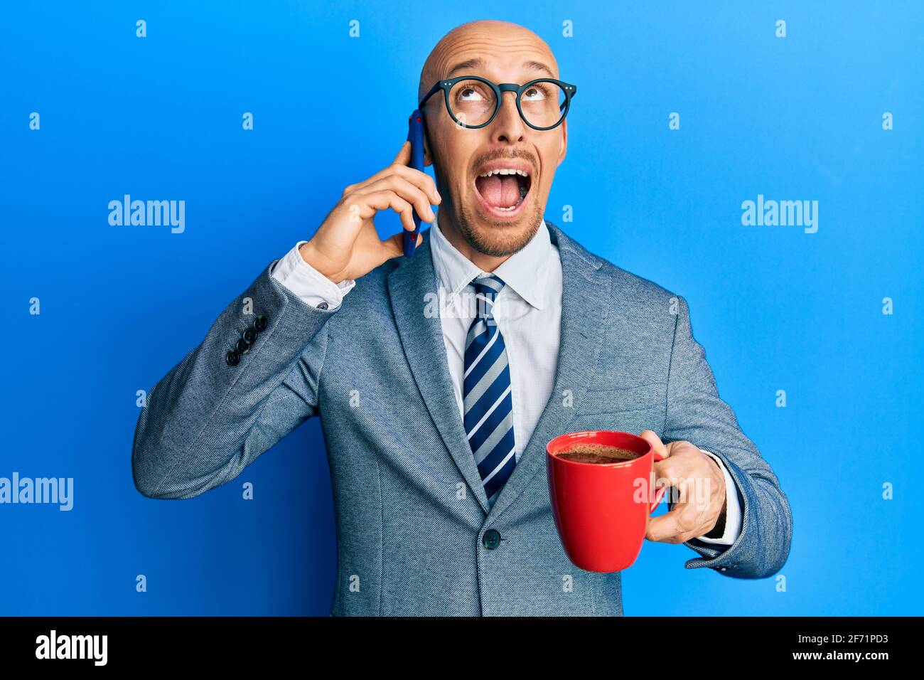 Bald man with beard using smartphone and drinking a cup of coffee angry ...