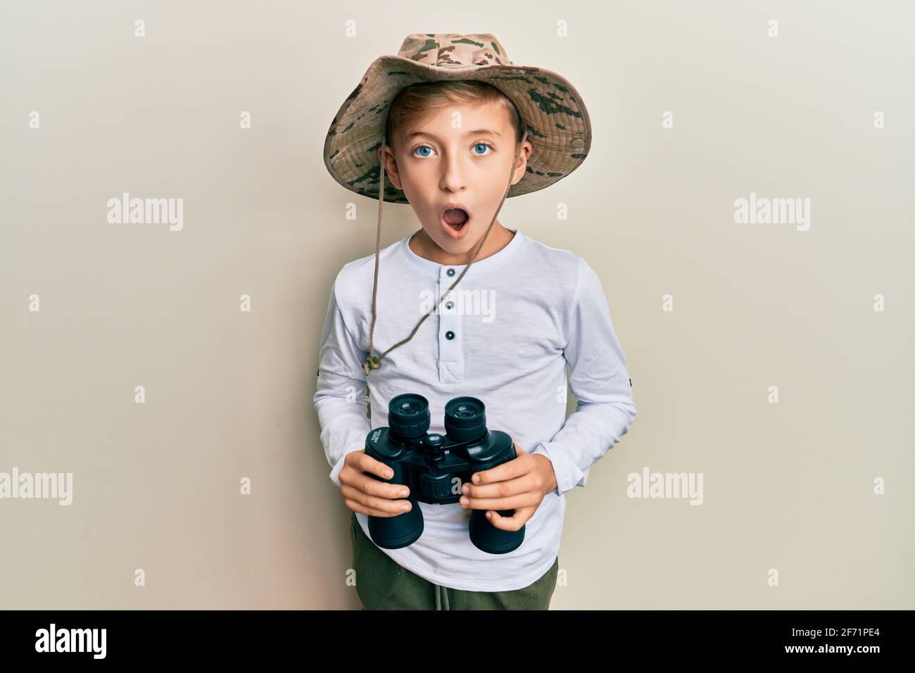 Little caucasian boy kid wearing explorer hat holding binoculars afraid ...